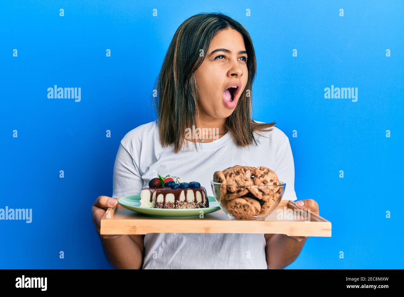 Young latin woman holding cake sweets and cookies angry and mad ...