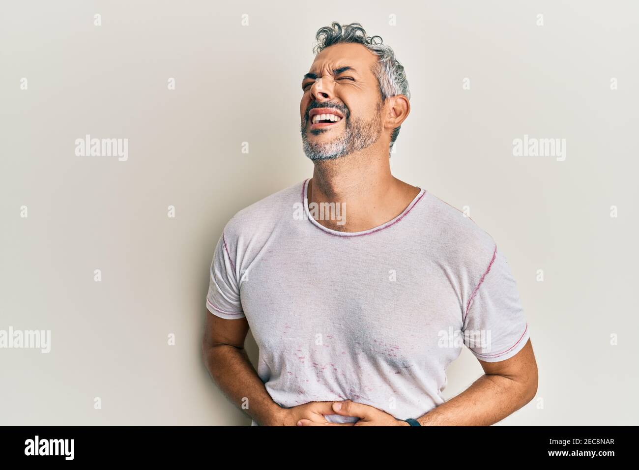 Middle age grey-haired man wearing casual clothes with hand on stomach ...
