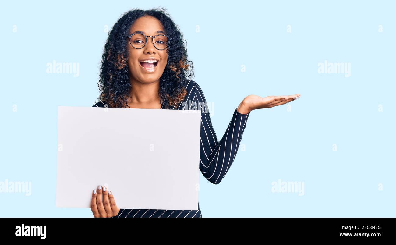 Young african american woman holding blank empty banner celebrating ...
