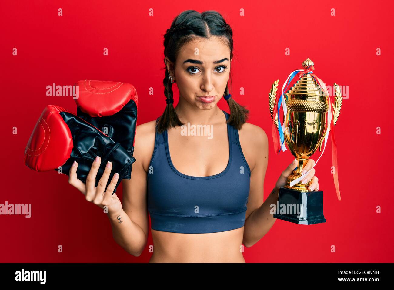 Young brunette girl holding boxer gloves and trophy depressed and worry ...