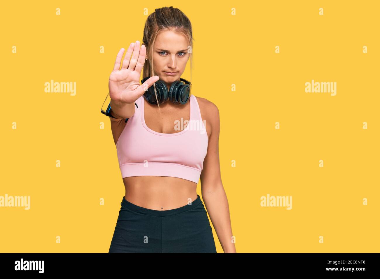 Young blonde woman wearing gym clothes and using headphones doing stop ...