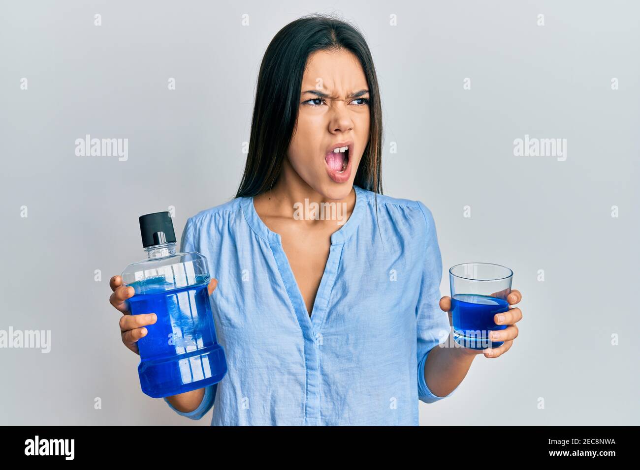 Young hispanic girl holding mouthwash for fresh breath angry and mad ...