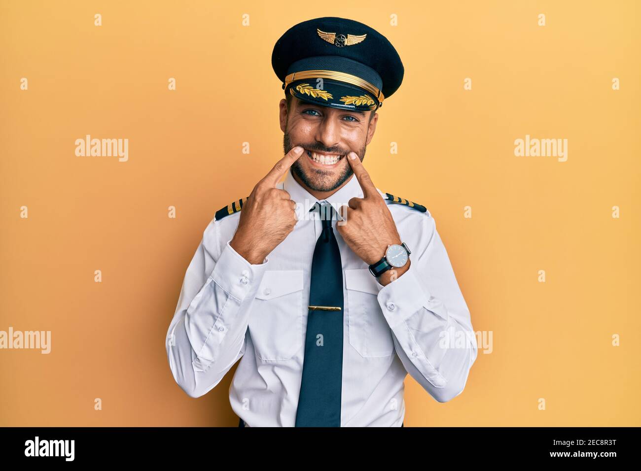 Handsome hispanic man wearing airplane pilot uniform smiling with open ...