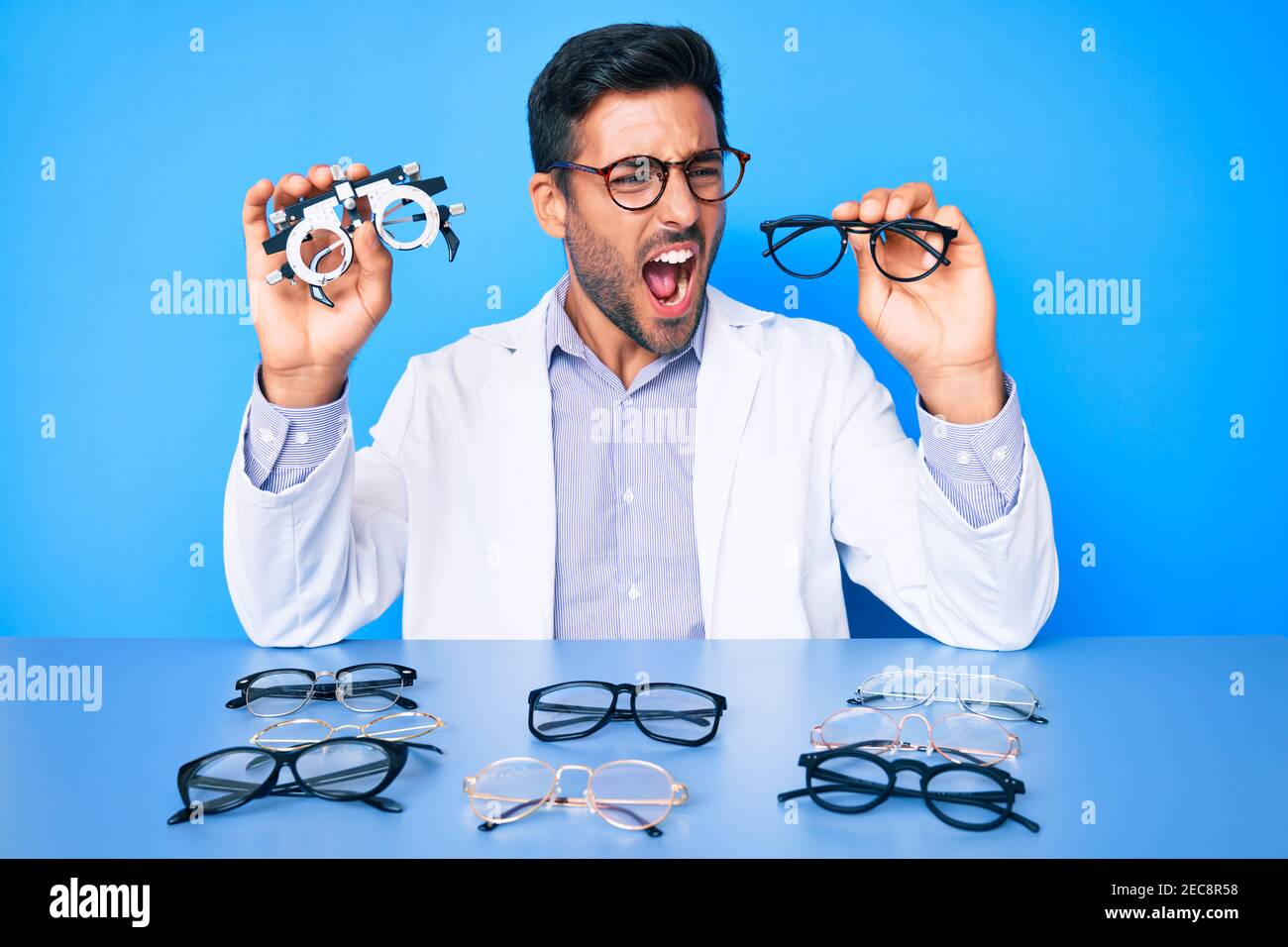 Young hispanic man with optometry glasses angry and mad screaming ...