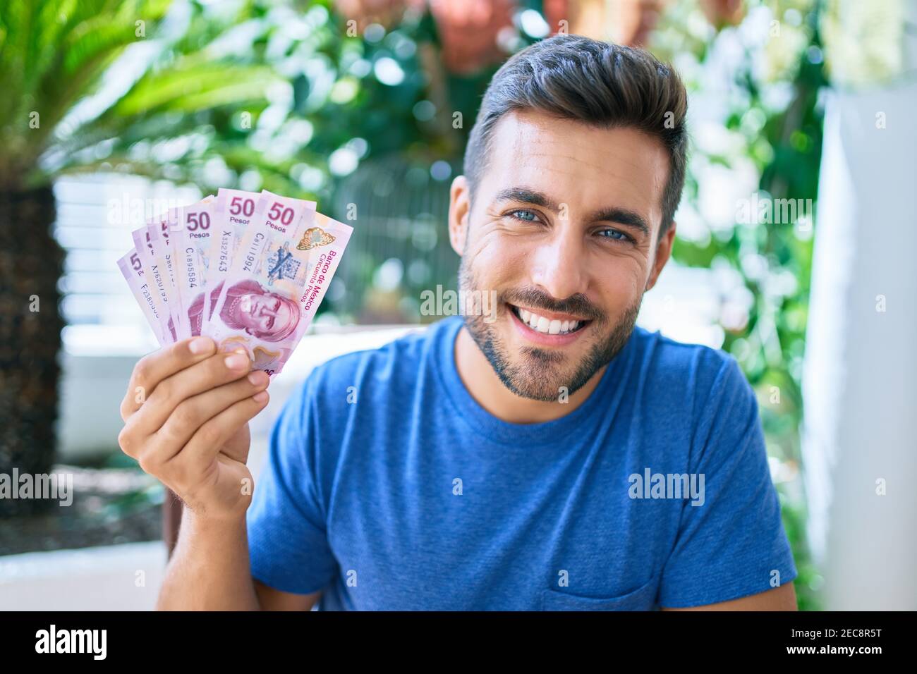 Young hispanic man smiling happy holding mexican pesos banknotes at the ...
