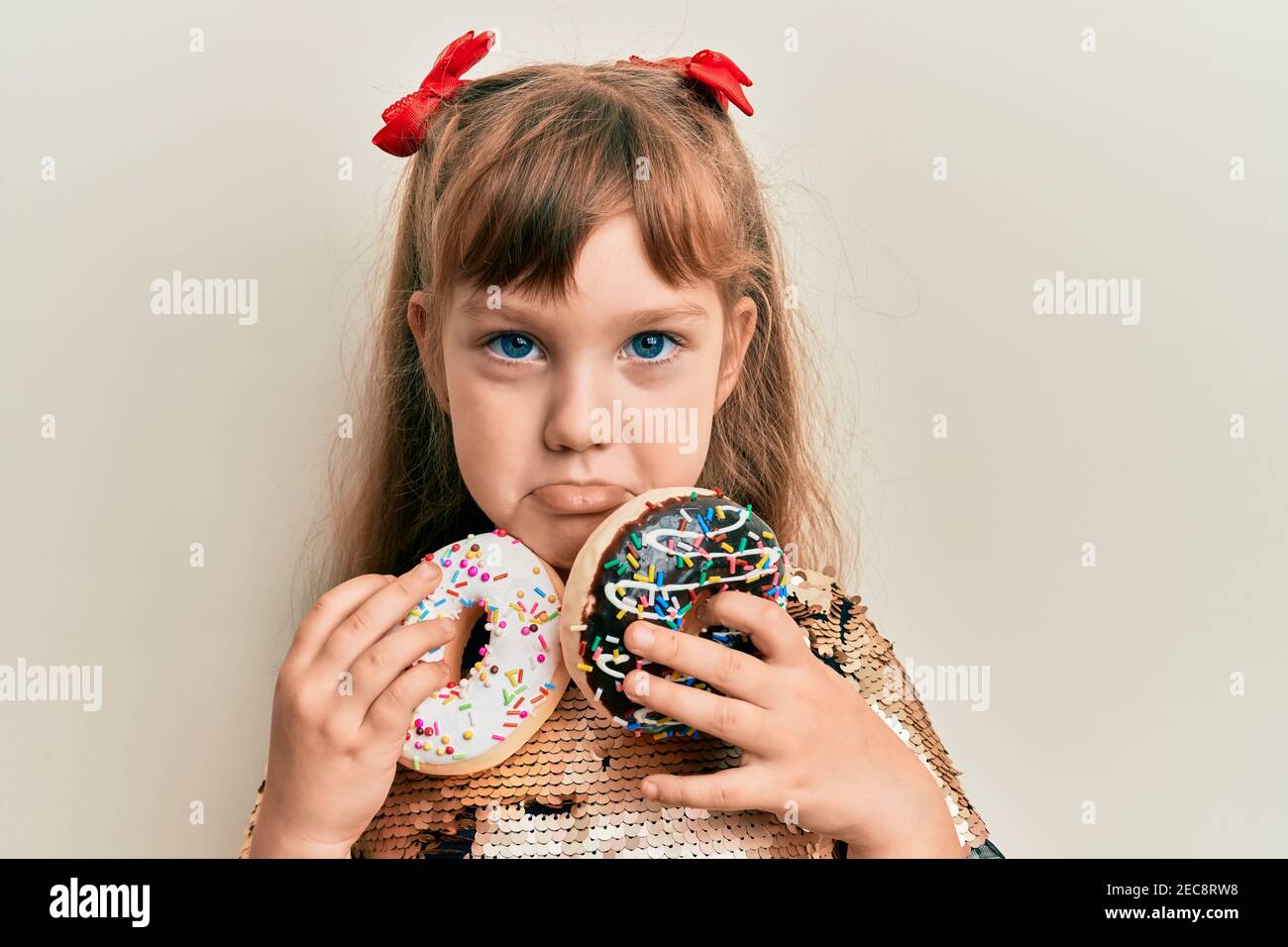 Little caucasian girl kid holding tasty colorful doughnuts depressed ...