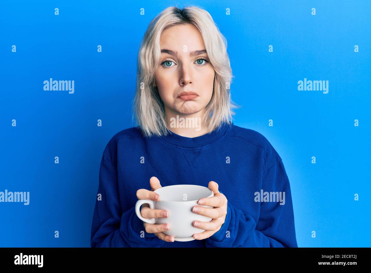 Young blonde girl drinking a cup of coffee depressed and worry for ...