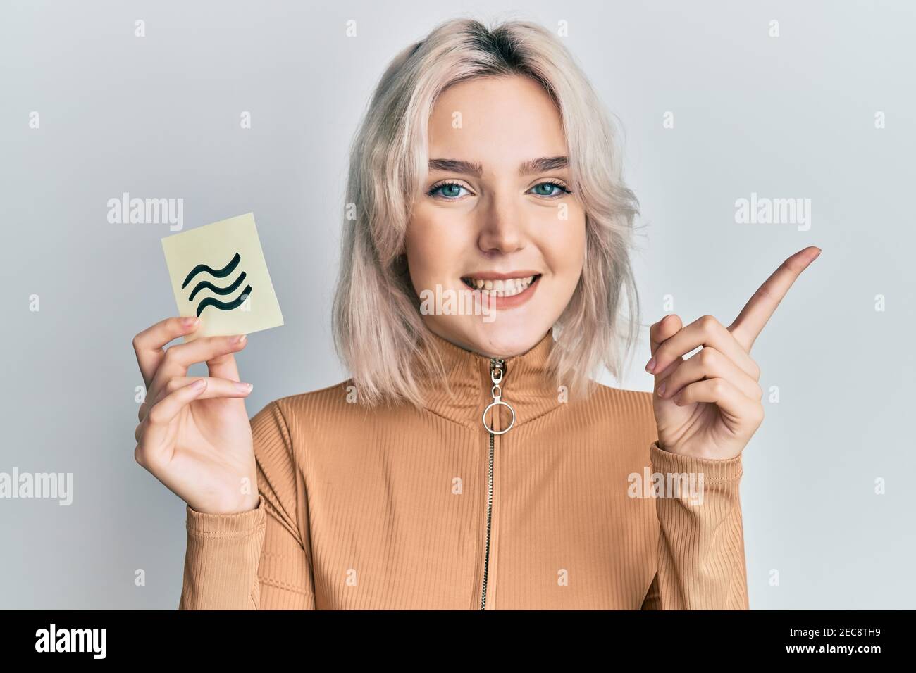 Young blonde girl holding paper with aquarius zodiac sign smiling happy ...