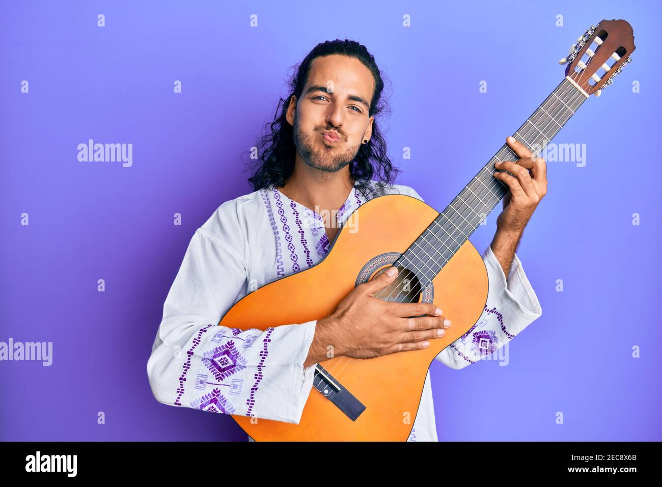 Young handsome man with long hair playing classical guitar puffing ...