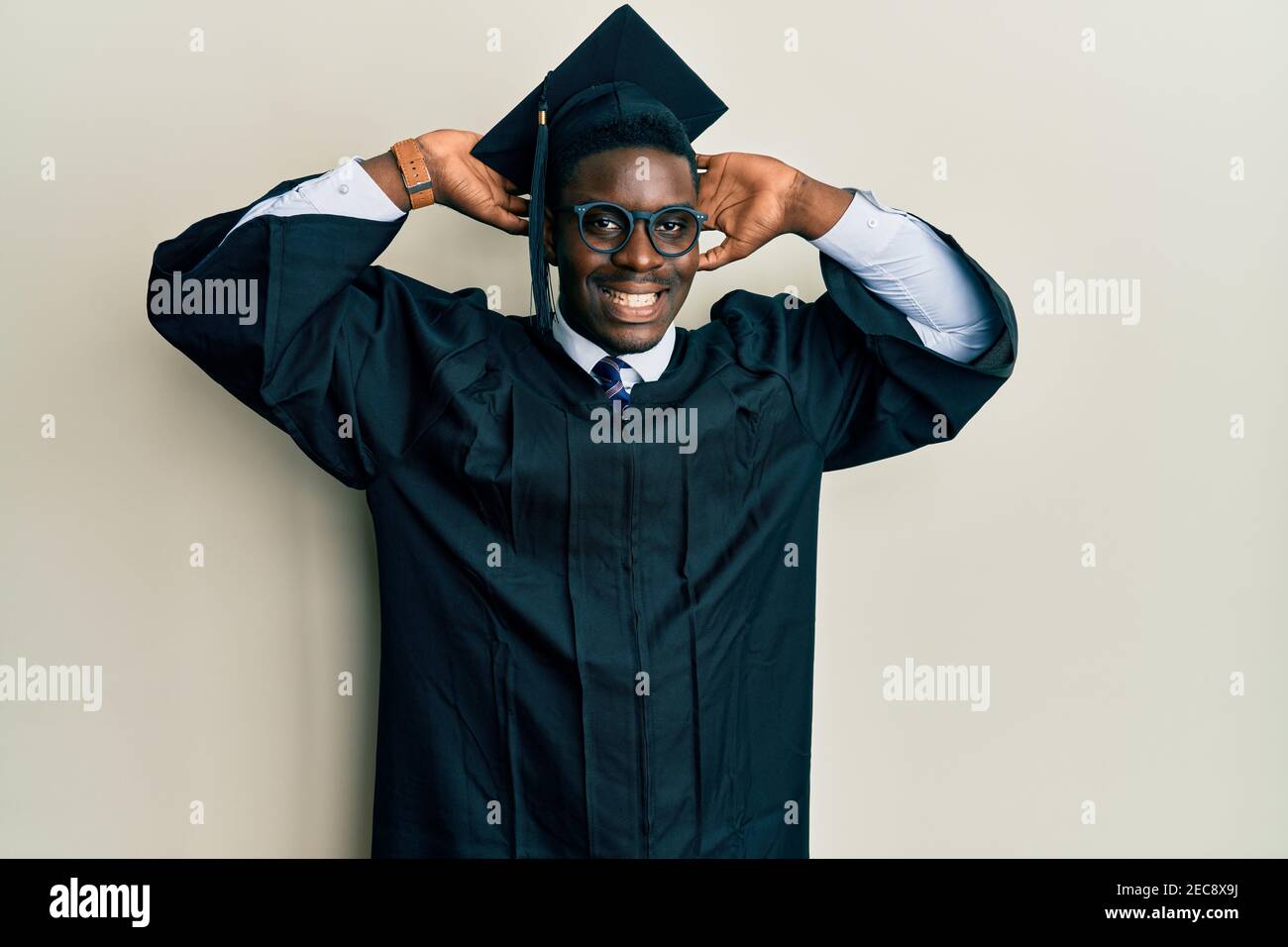 Handsome black man wearing graduation cap and ceremony robe relaxing ...