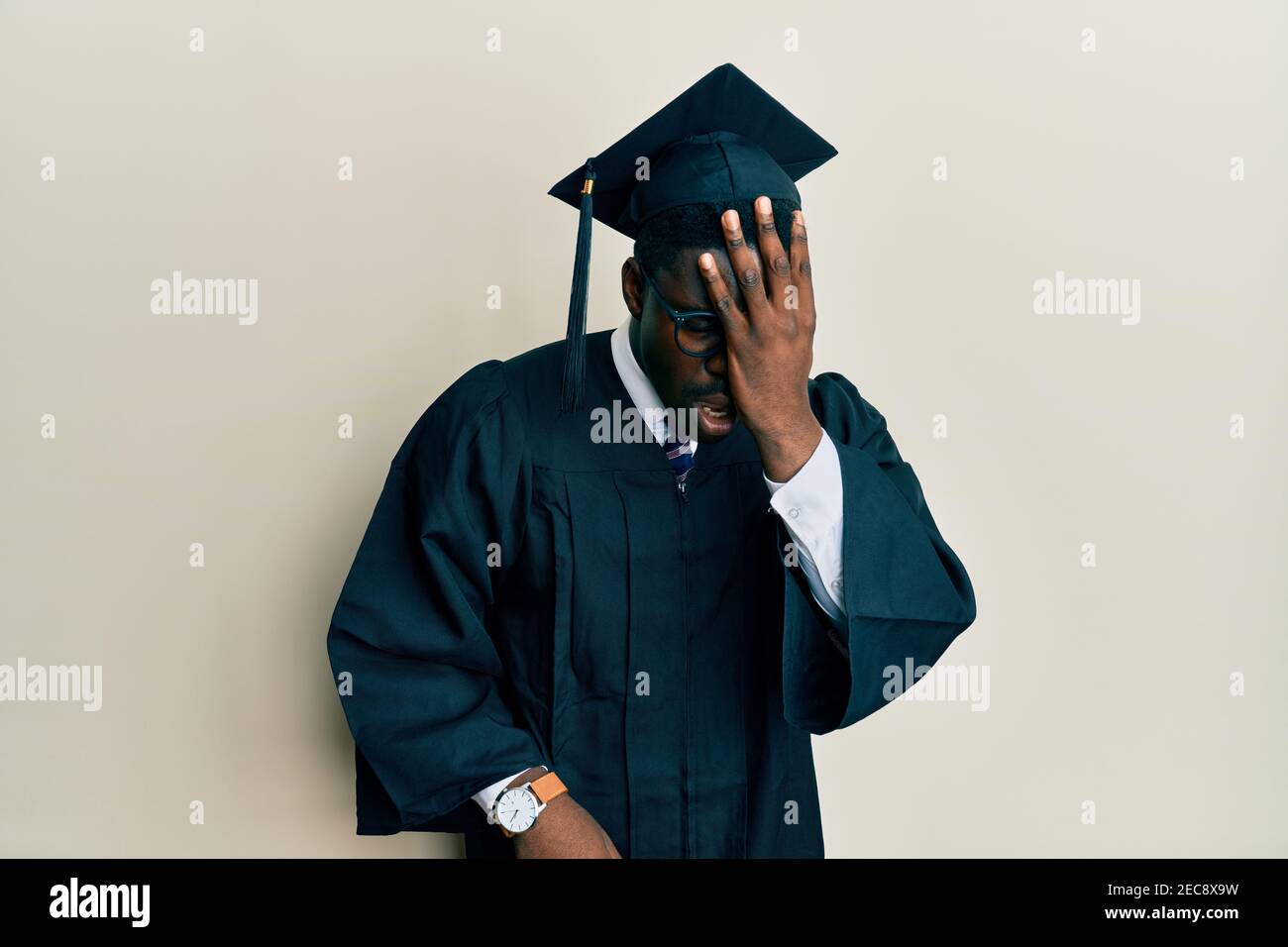 Handsome black man wearing graduation cap and ceremony robe yawning ...