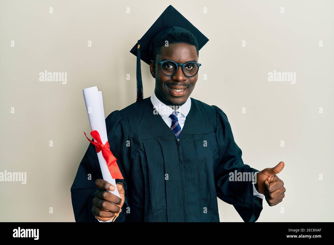 Handsome black man wearing graduation cap and ceremony robe holding ...