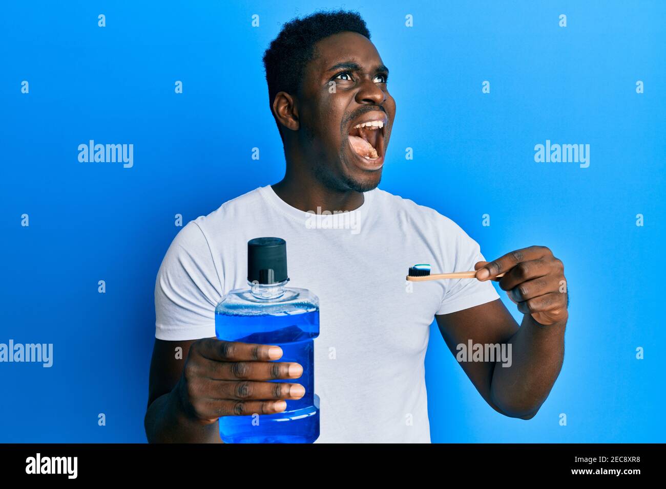 Handsome black man holding mouthwash and toothbrush for fresh breath ...