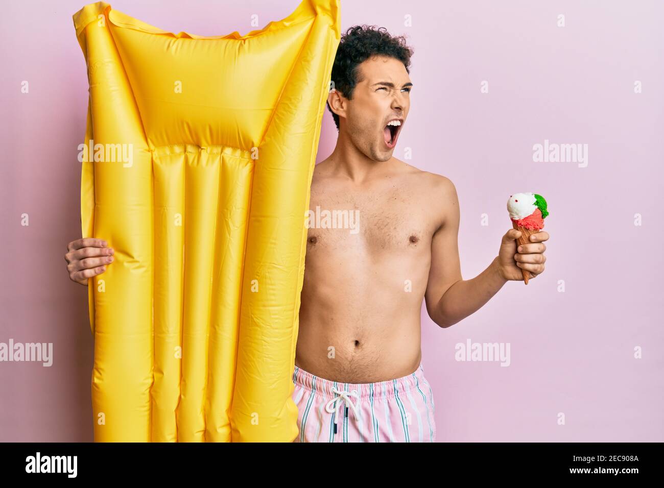 Young handsome man wearing swimsuit holding summer mattress float and ...