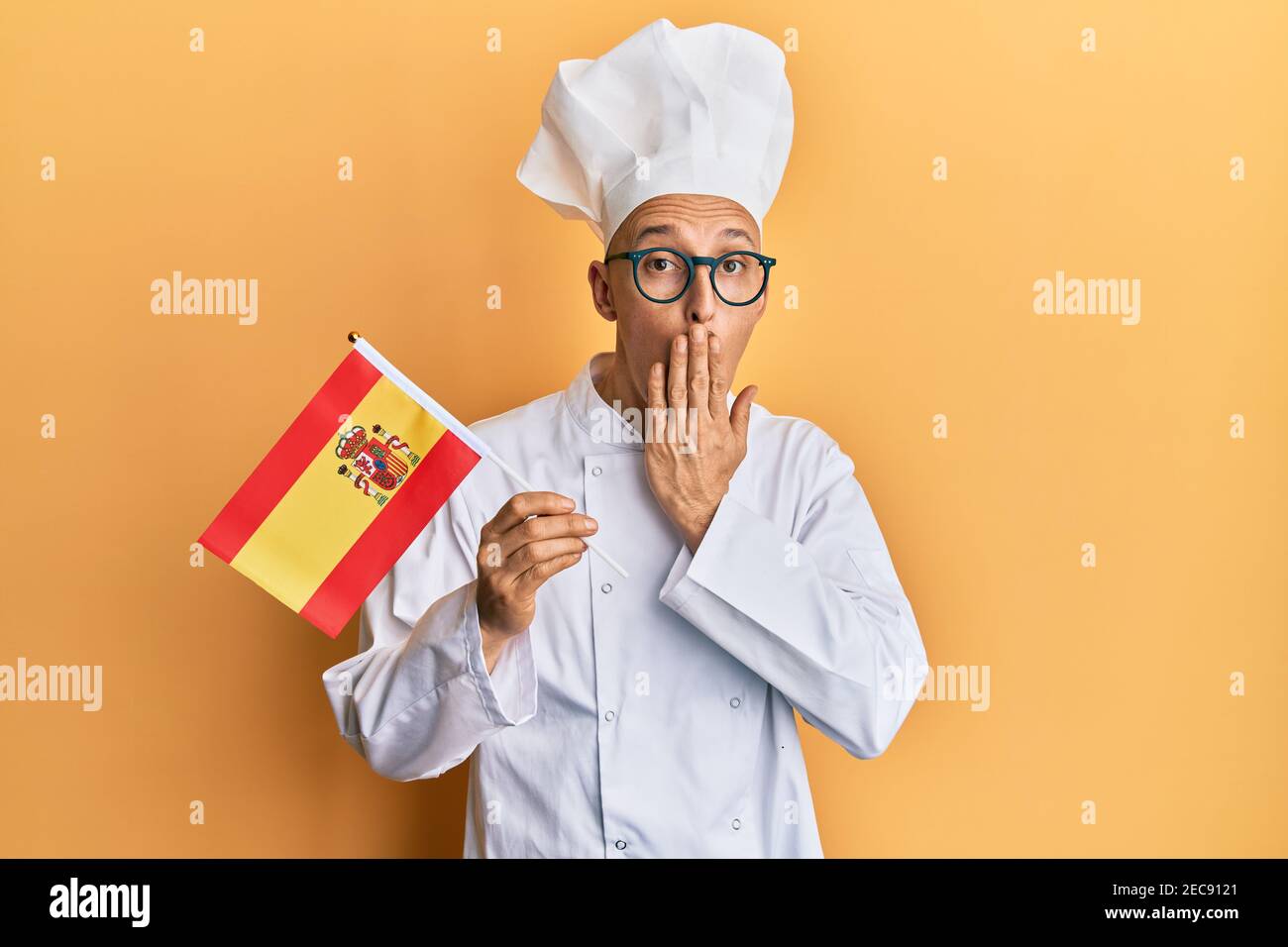 Bald man with beard wearing professional cook apron holding spanish ...