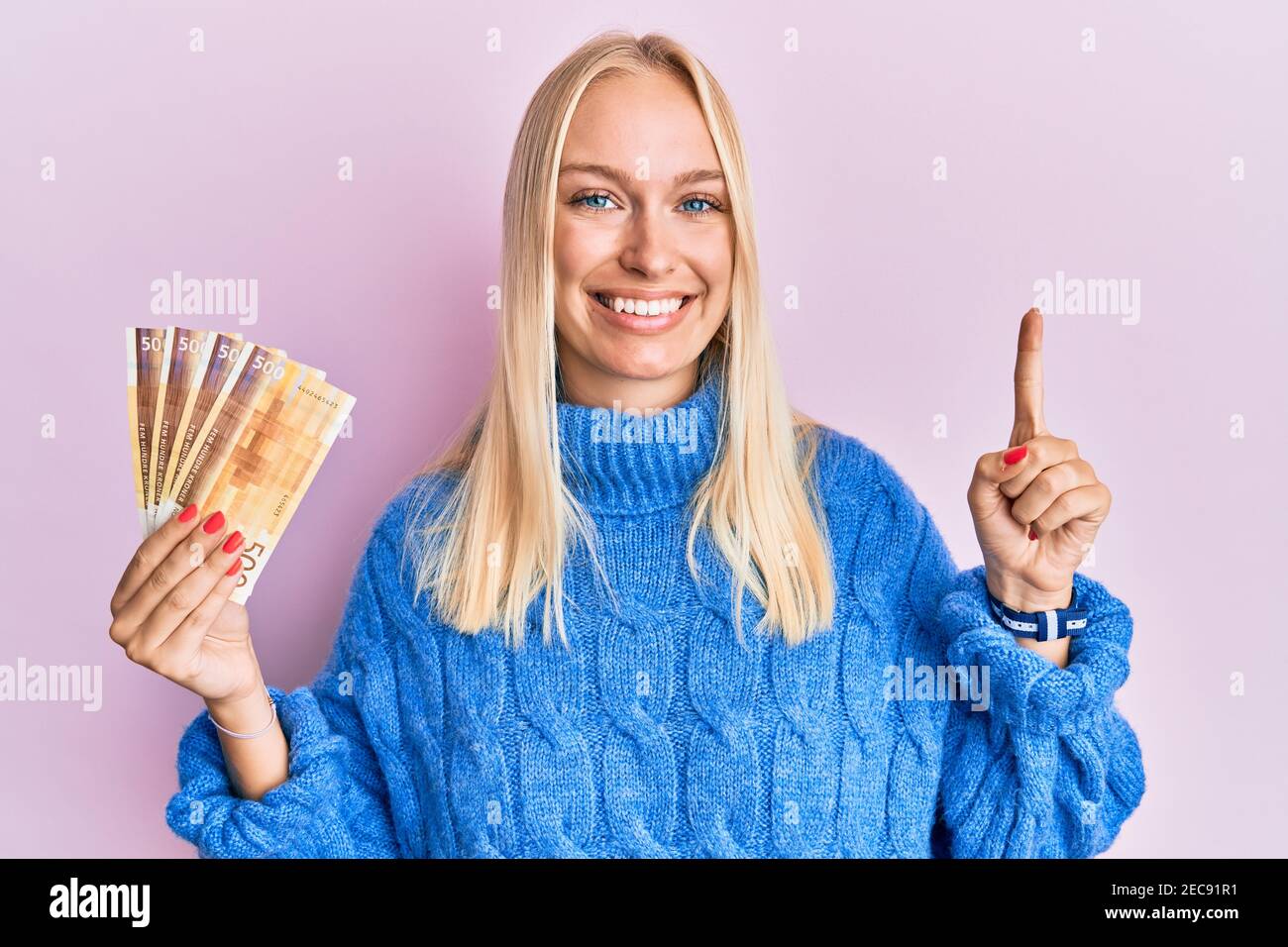 Young blonde girl holding 100 norwegian krone banknotes smiling with an ...