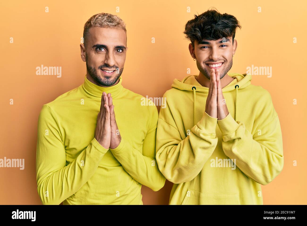 Homosexual gay couple standing together wearing yellow clothes praying ...