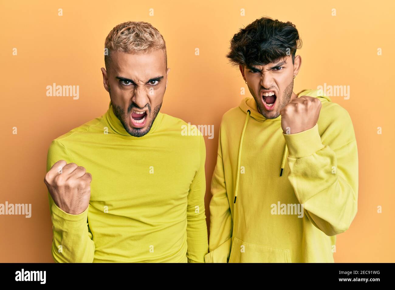 Homosexual gay couple standing together wearing yellow clothes angry ...