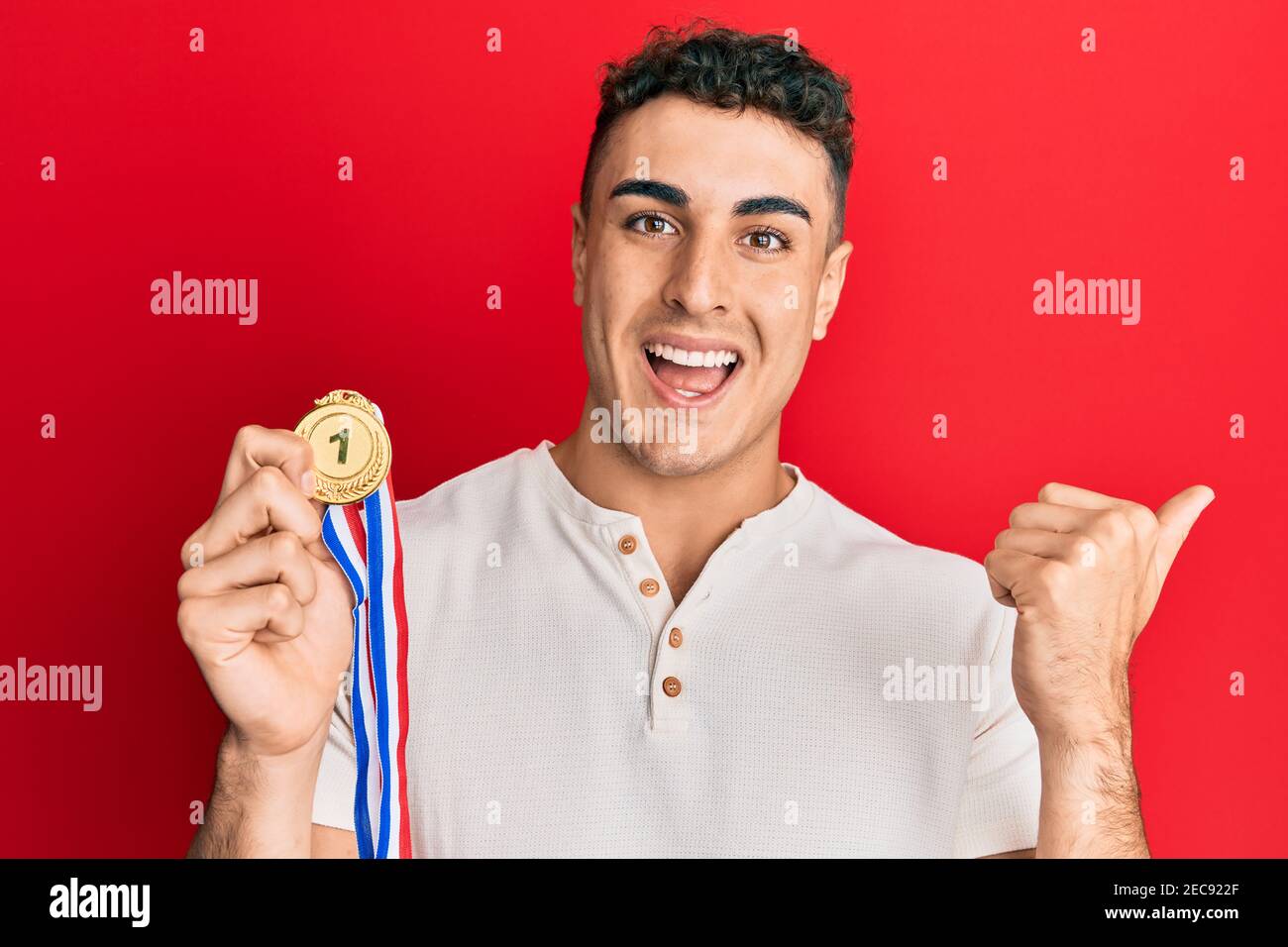 Hispanic young man holding first place medal pointing thumb up to the ...