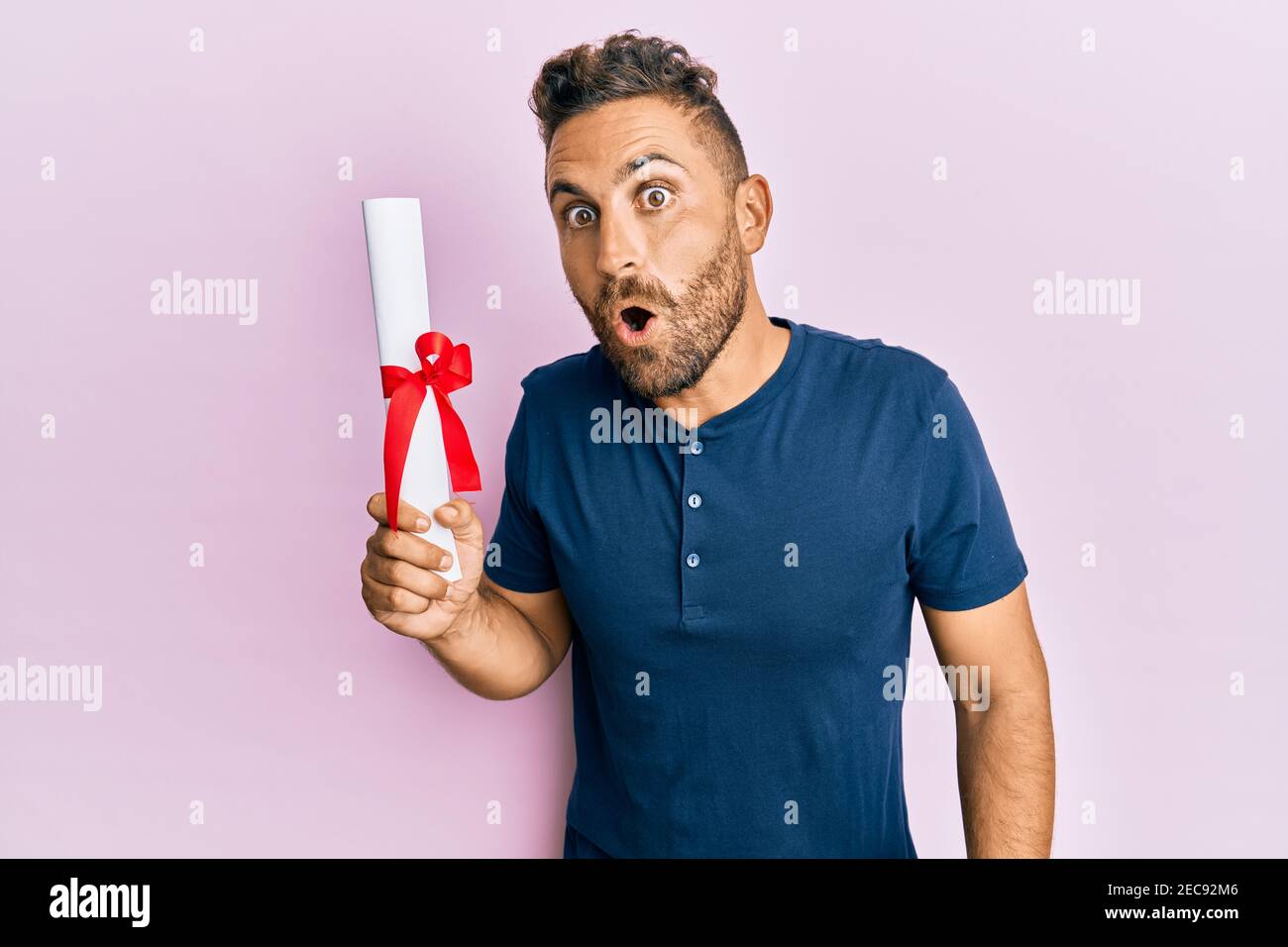 Handsome man with beard holding graduate degree diploma scared and ...