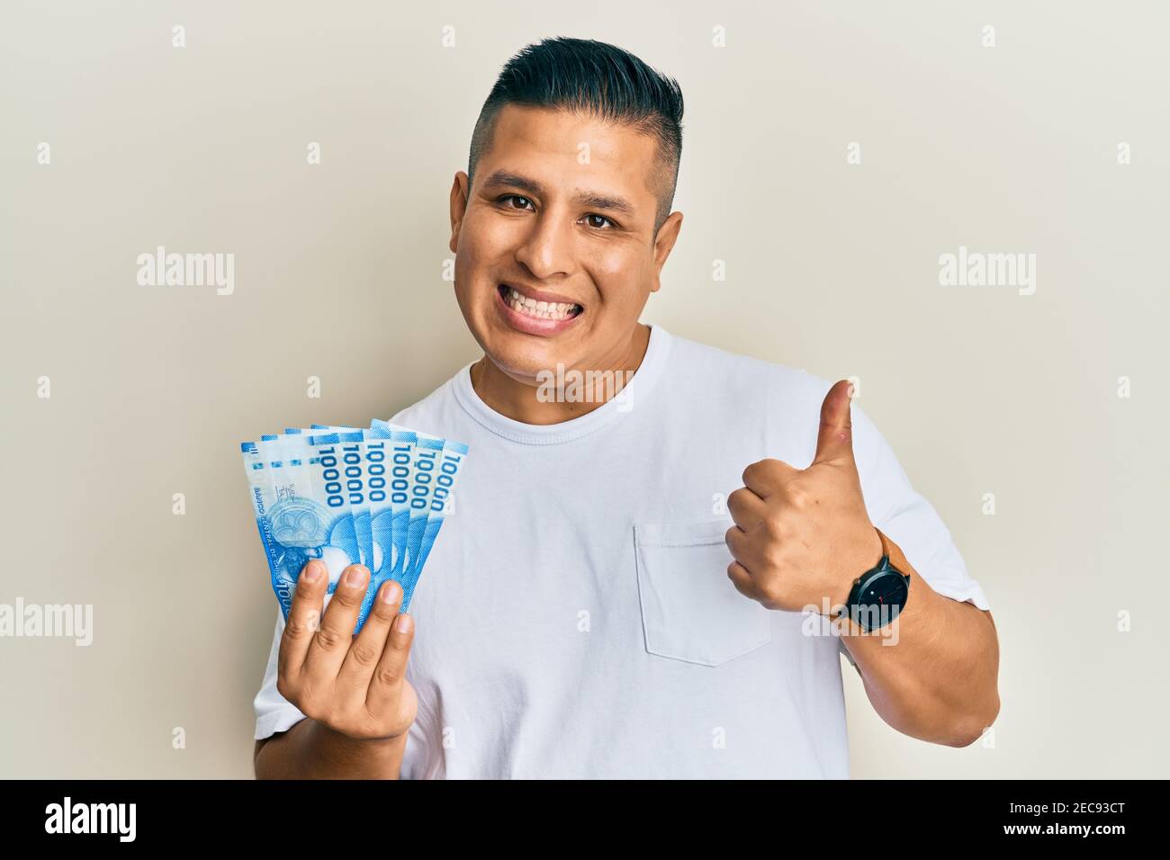 Young latin man holding 10000 chilean pesos smiling happy and positive ...