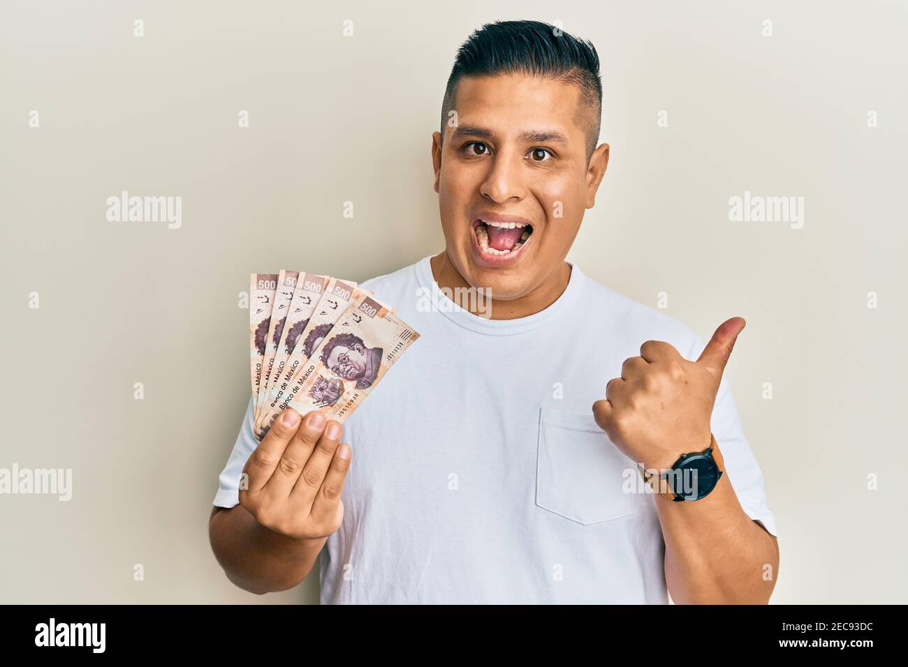 Young latin man holding 500 mexican pesos banknotes pointing thumb up ...