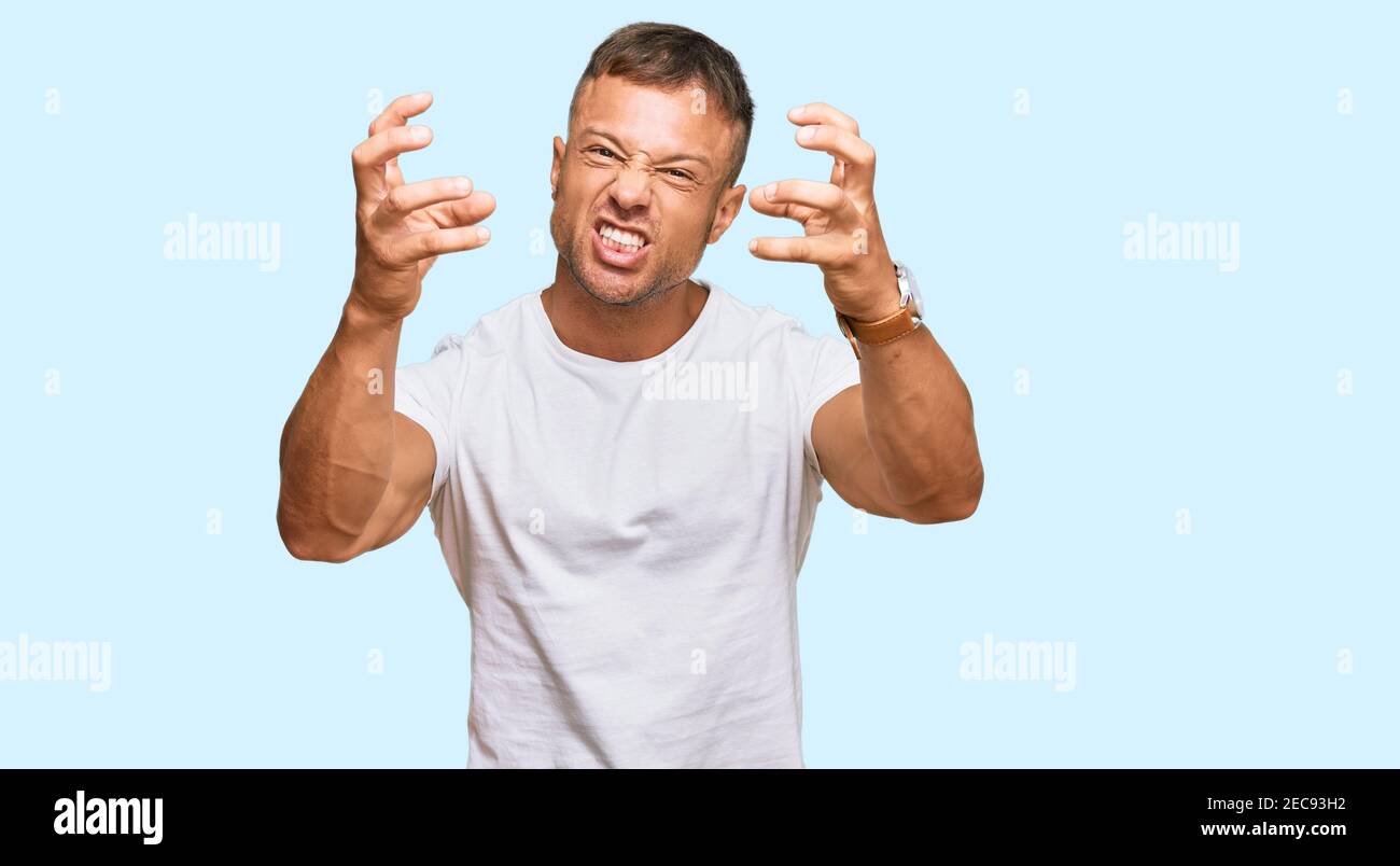 Handsome muscle man wearing casual white tshirt shouting frustrated ...