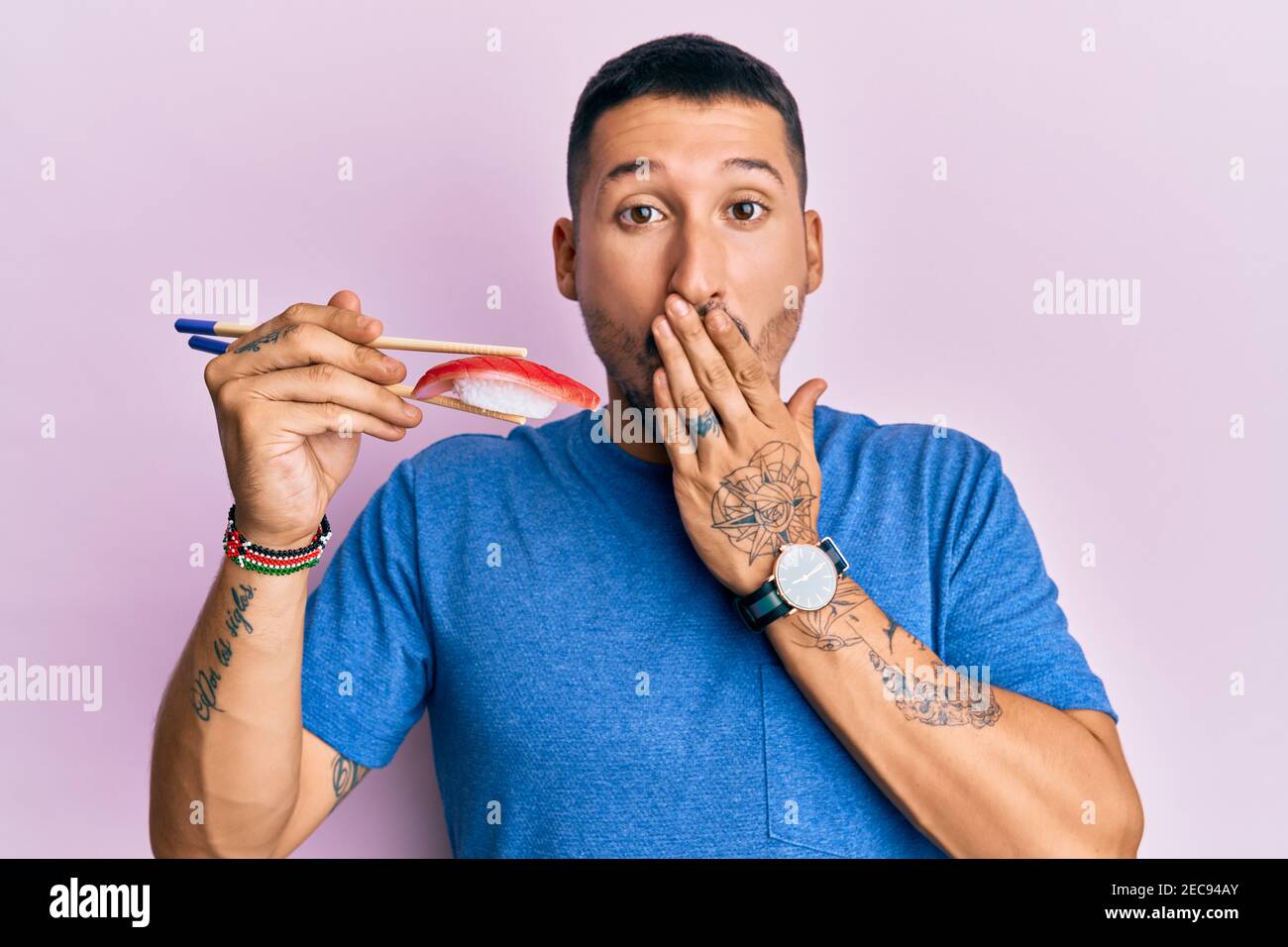 Handsome man with tattoos eating tuna sushi using chopsticks covering ...