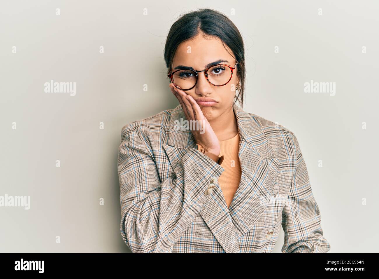 Young brunette woman wearing business jacket and glasses thinking ...