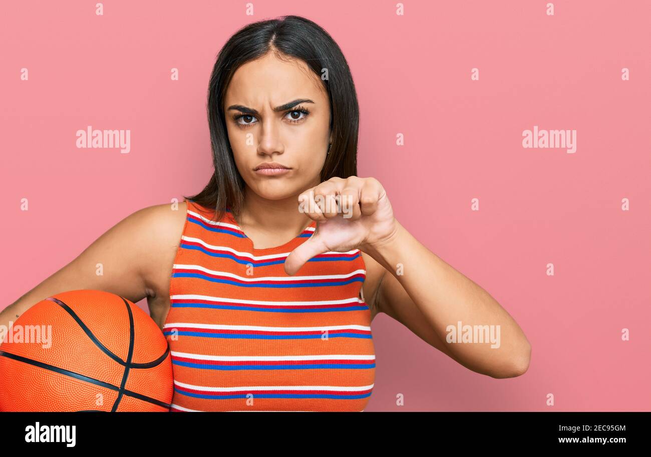 Young brunette woman holding basketball ball with angry face, negative ...
