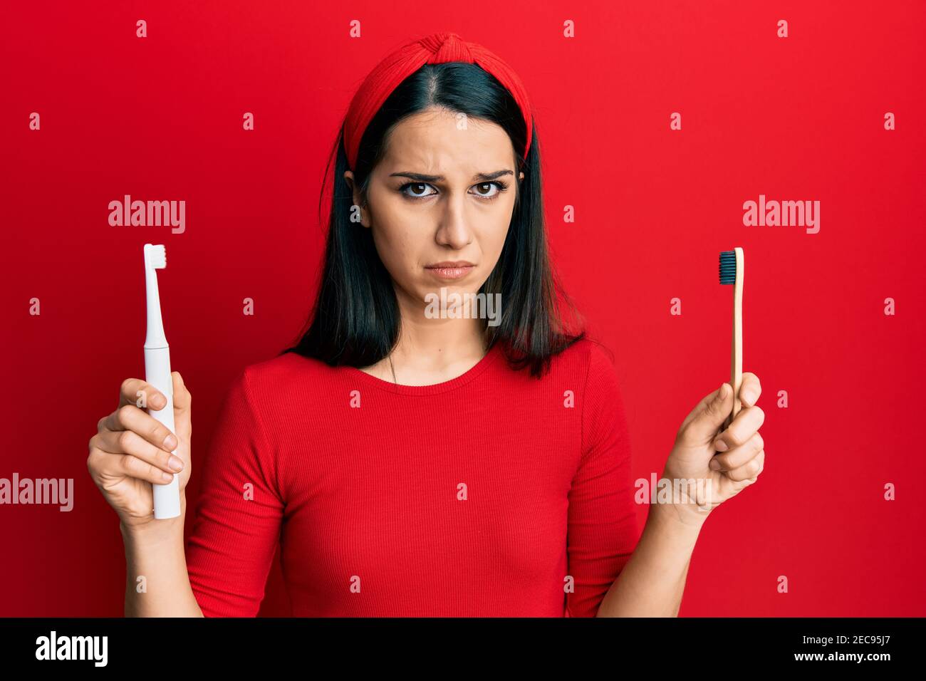 Young hispanic woman choosing electric toothbrush or normal teethbrush ...