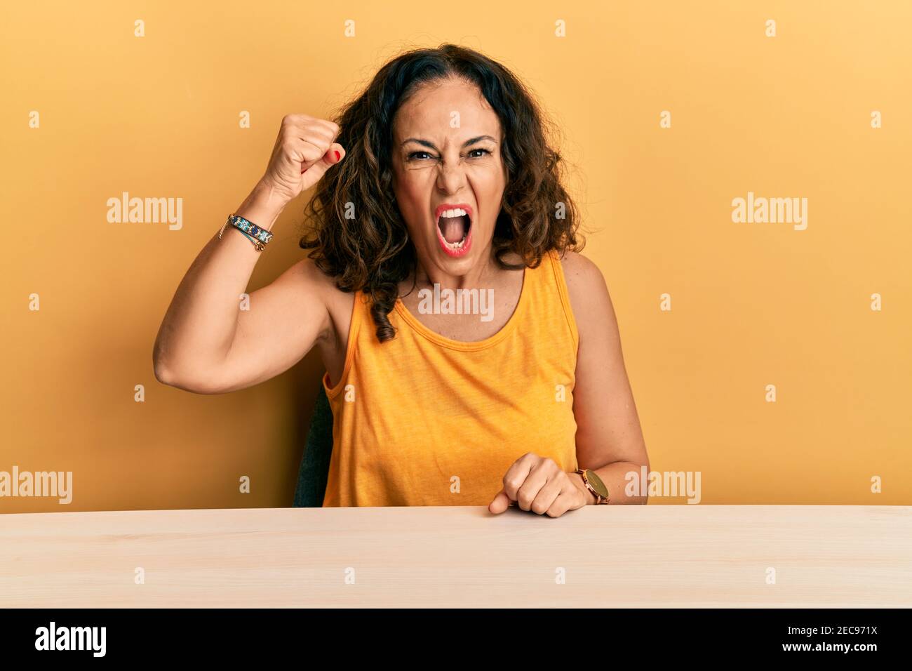 Beautiful middle age woman wearing casual clothes sitting on the table ...