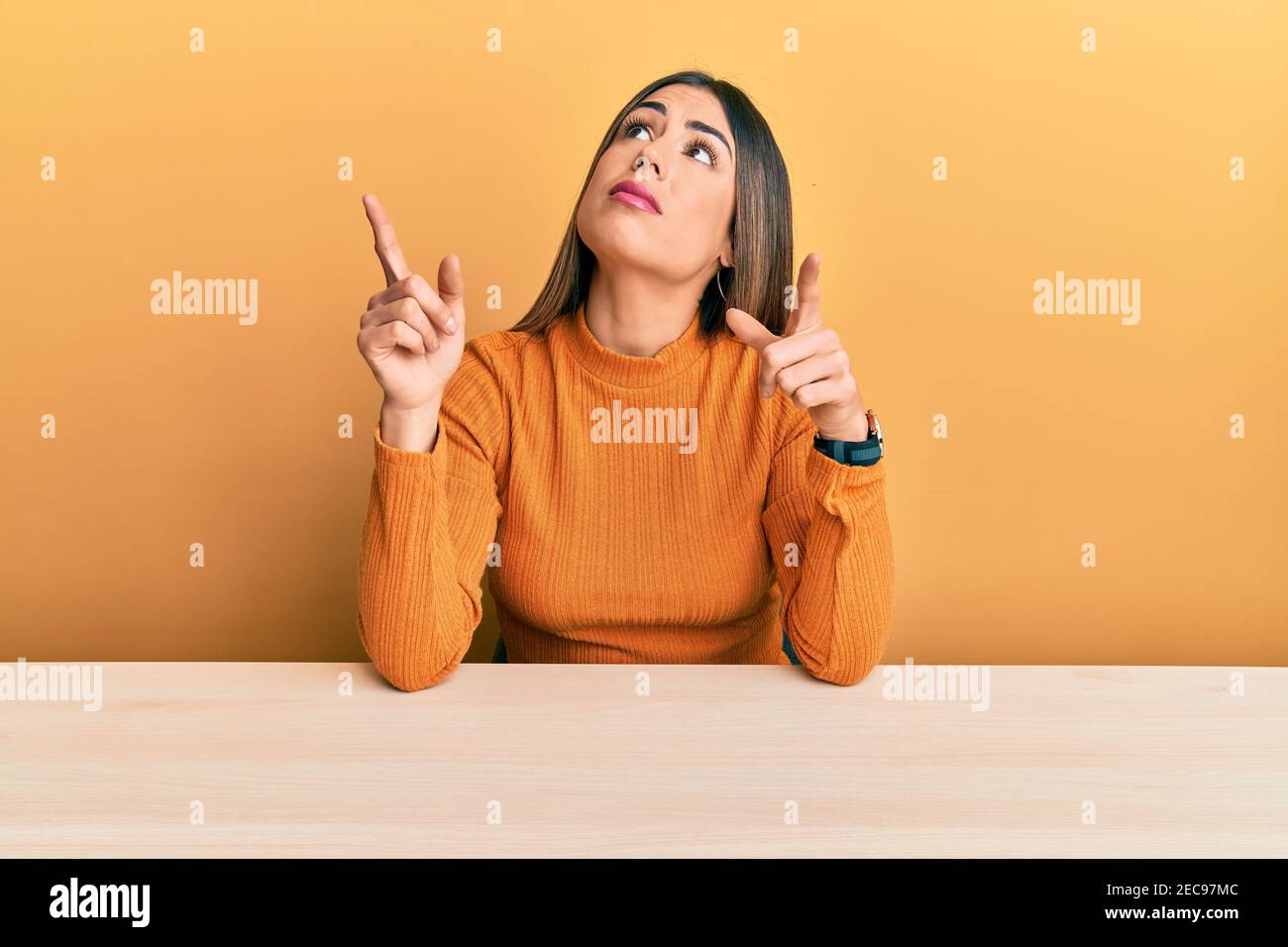 Young hispanic woman wearing casual clothes sitting on the table ...
