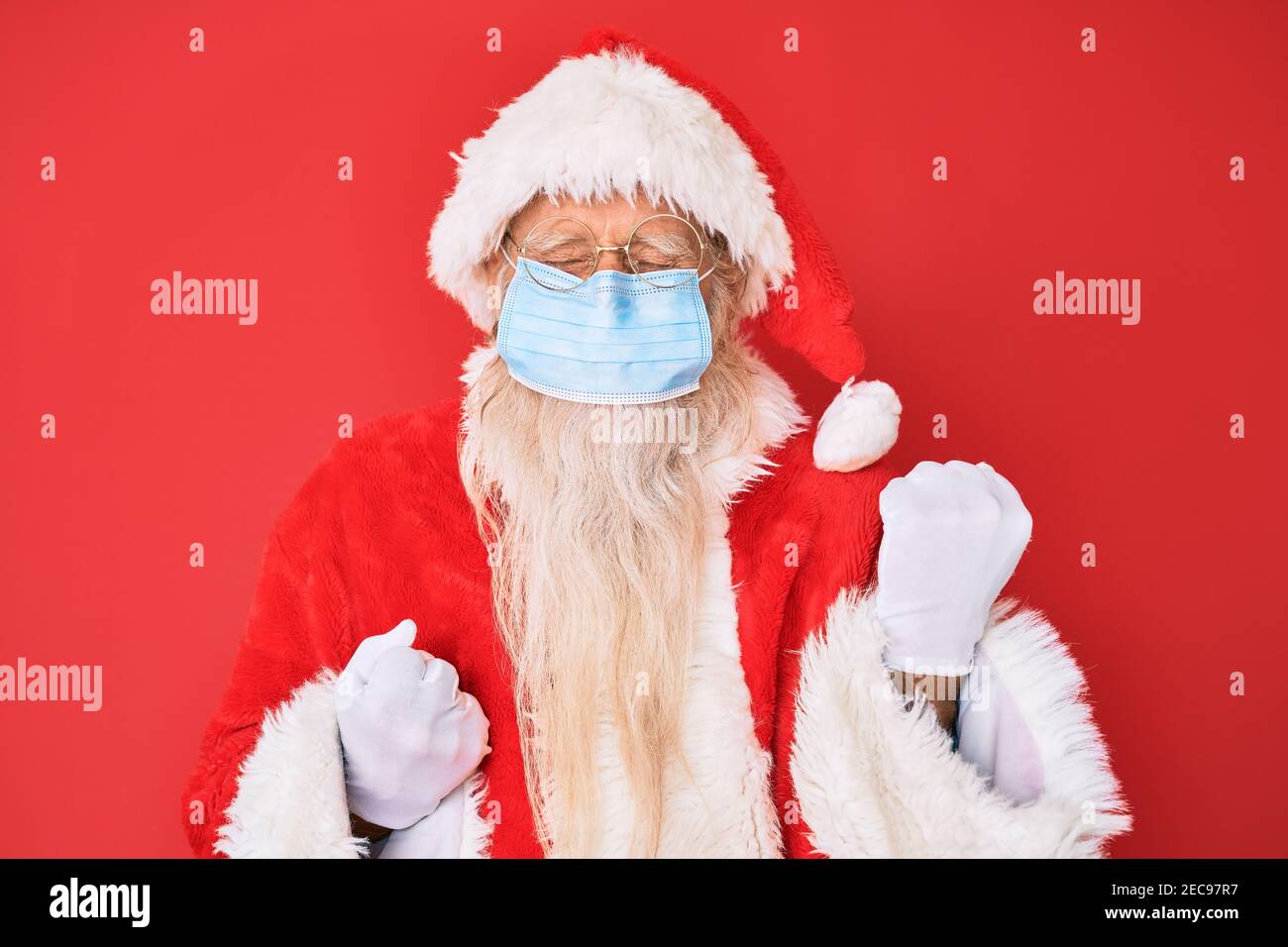 Old senior man wearing santa claus costume wearing safety mask ...