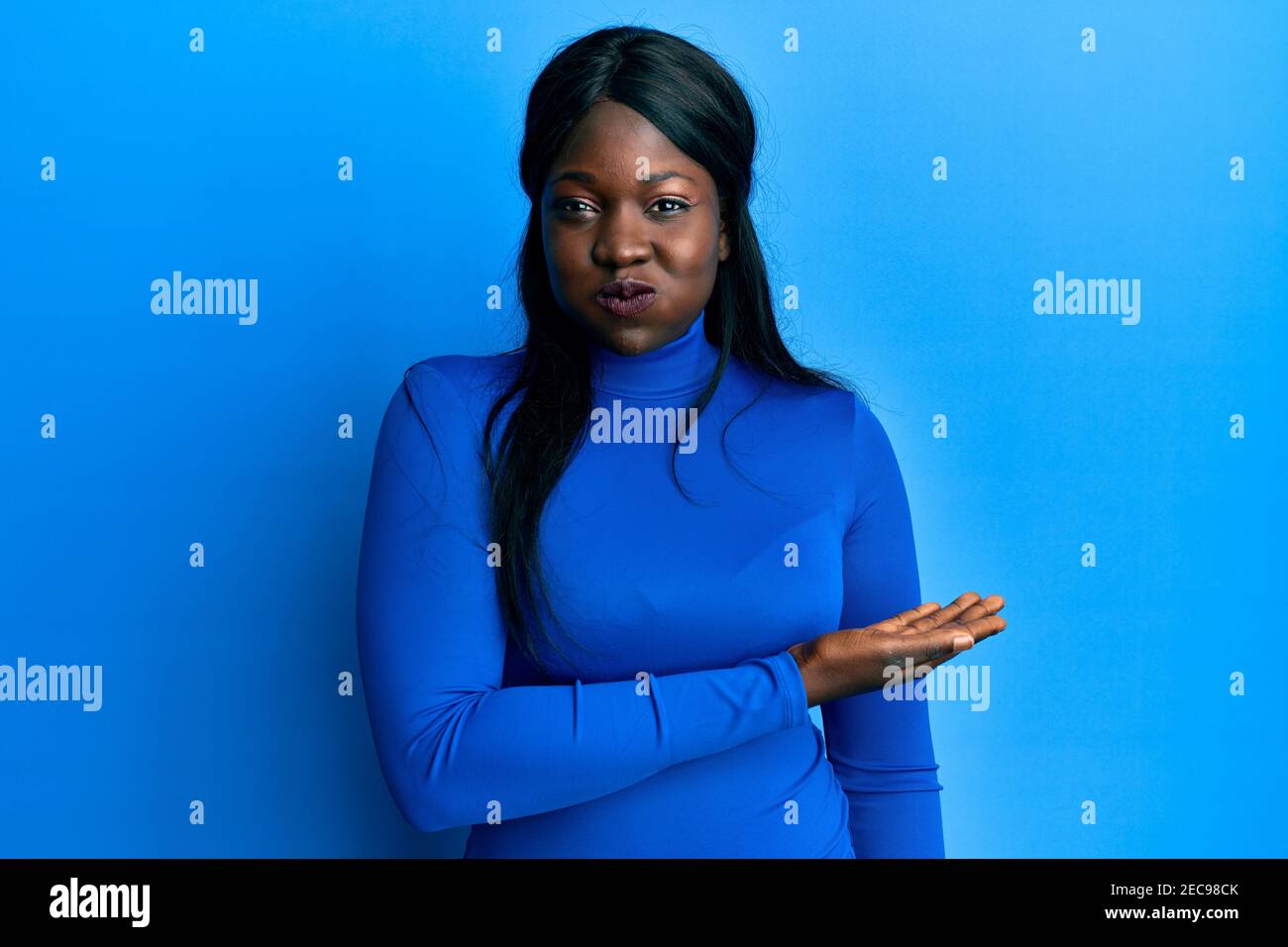 African young woman presenting with open palm to the side puffing ...