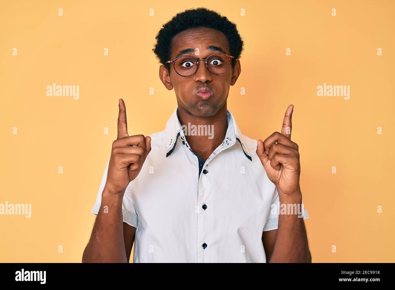African handsome man pointing up with fingers puffing cheeks with funny ...