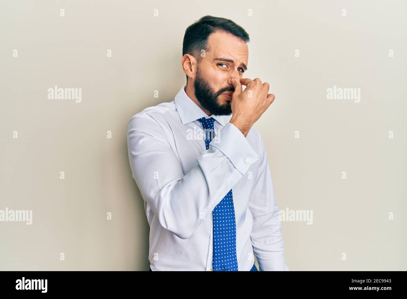 Young man with beard wearing business tie smelling something stinky and ...