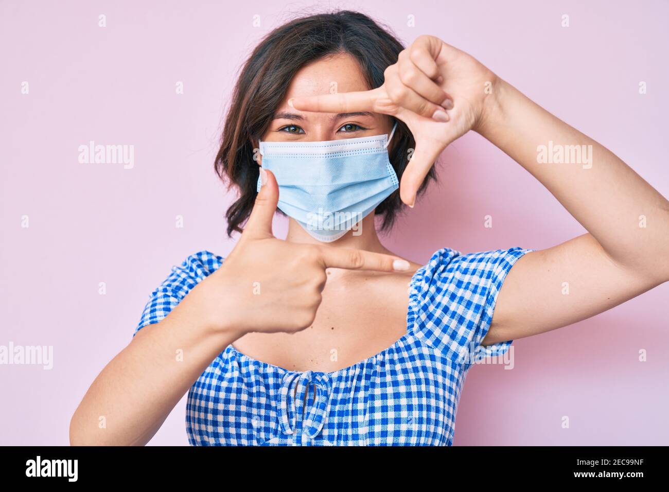 Young beautiful woman wearing medical mask smiling making frame with ...