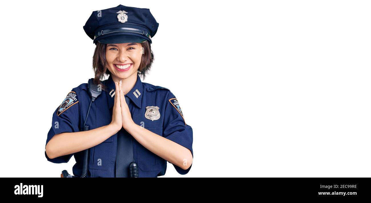 Young beautiful girl wearing police uniform praying with hands together ...