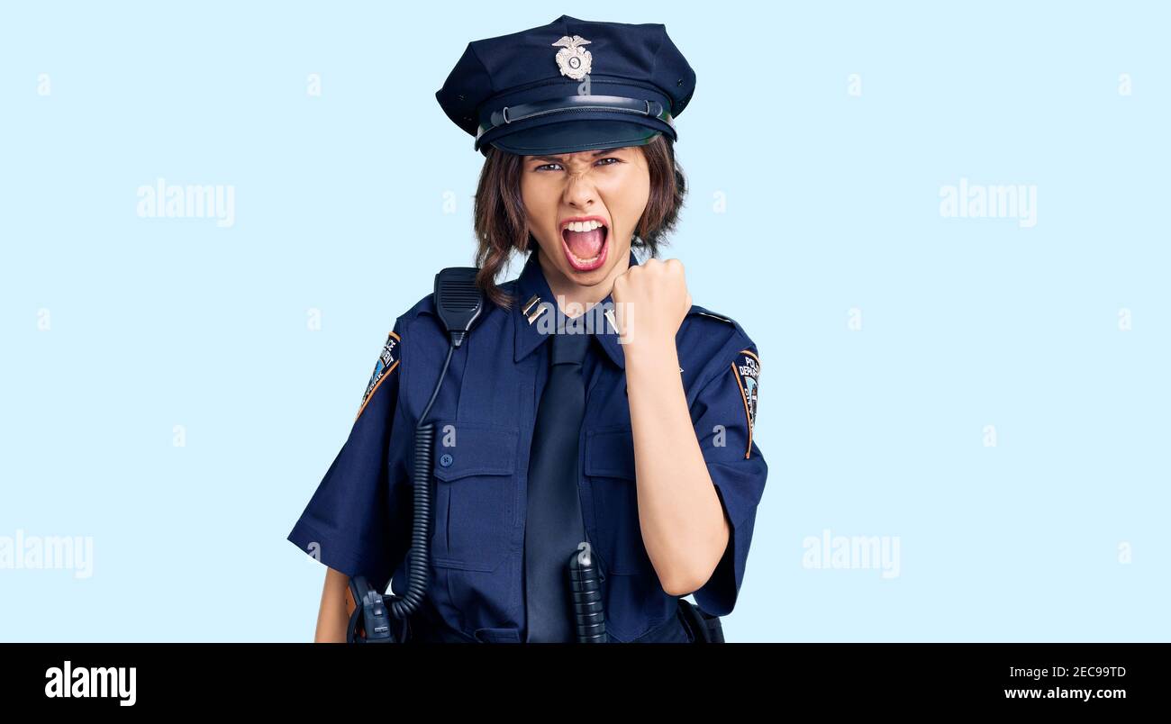 Young beautiful girl wearing police uniform angry and mad raising fist ...