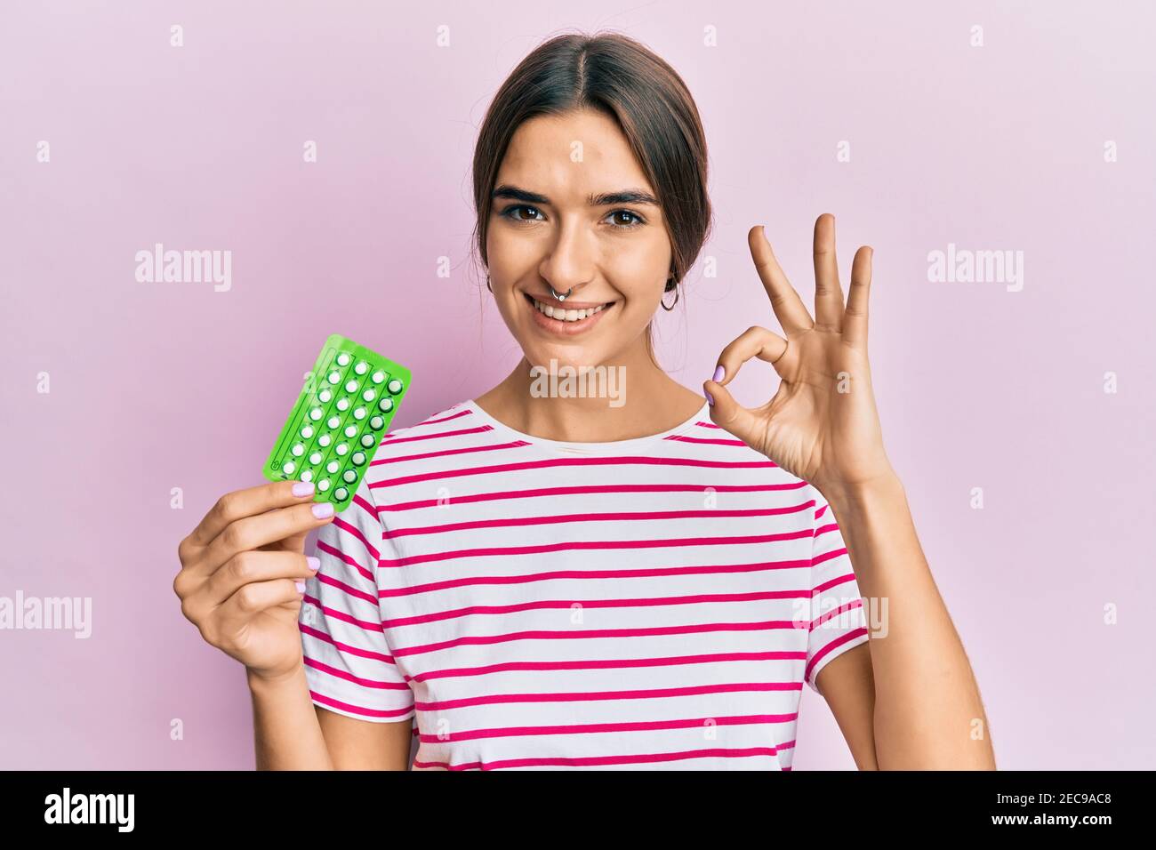 Young hispanic woman holding birth control pills doing ok sign with ...