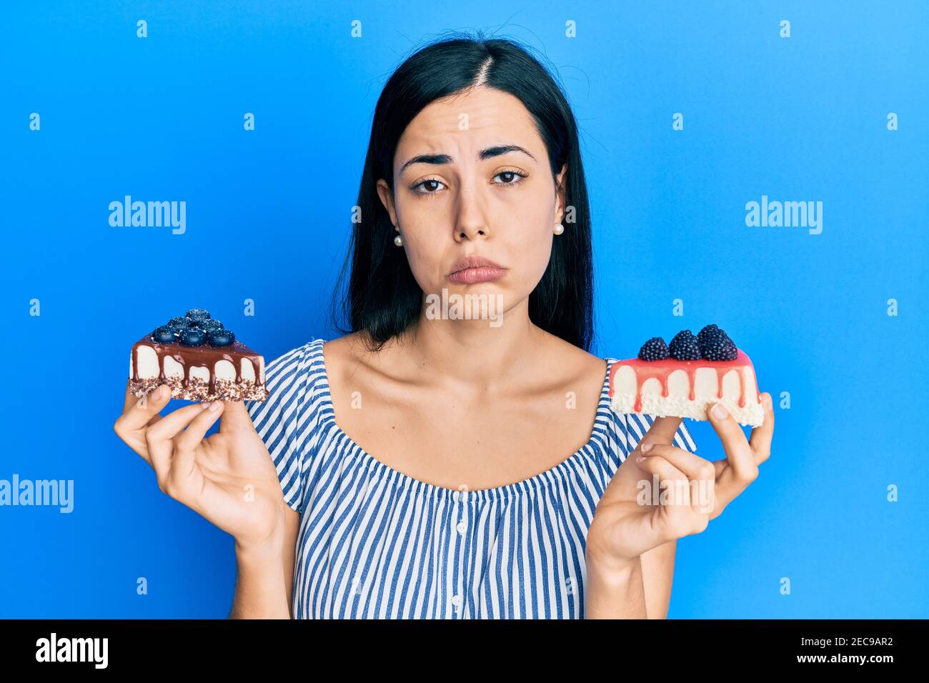 Beautiful young woman holding cake slices depressed and worry for ...