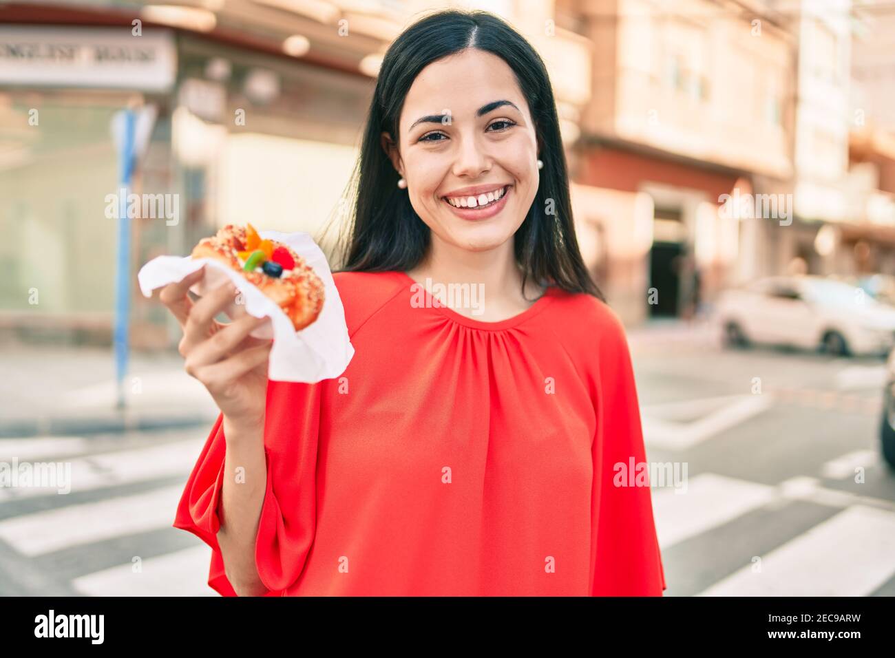Young latin girl smiling happy eating sweet walking at the city Stock ...