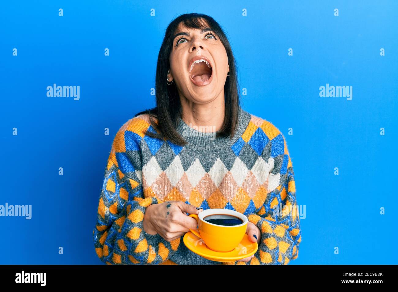 Young hispanic woman drinking a cup of coffee angry and mad screaming ...