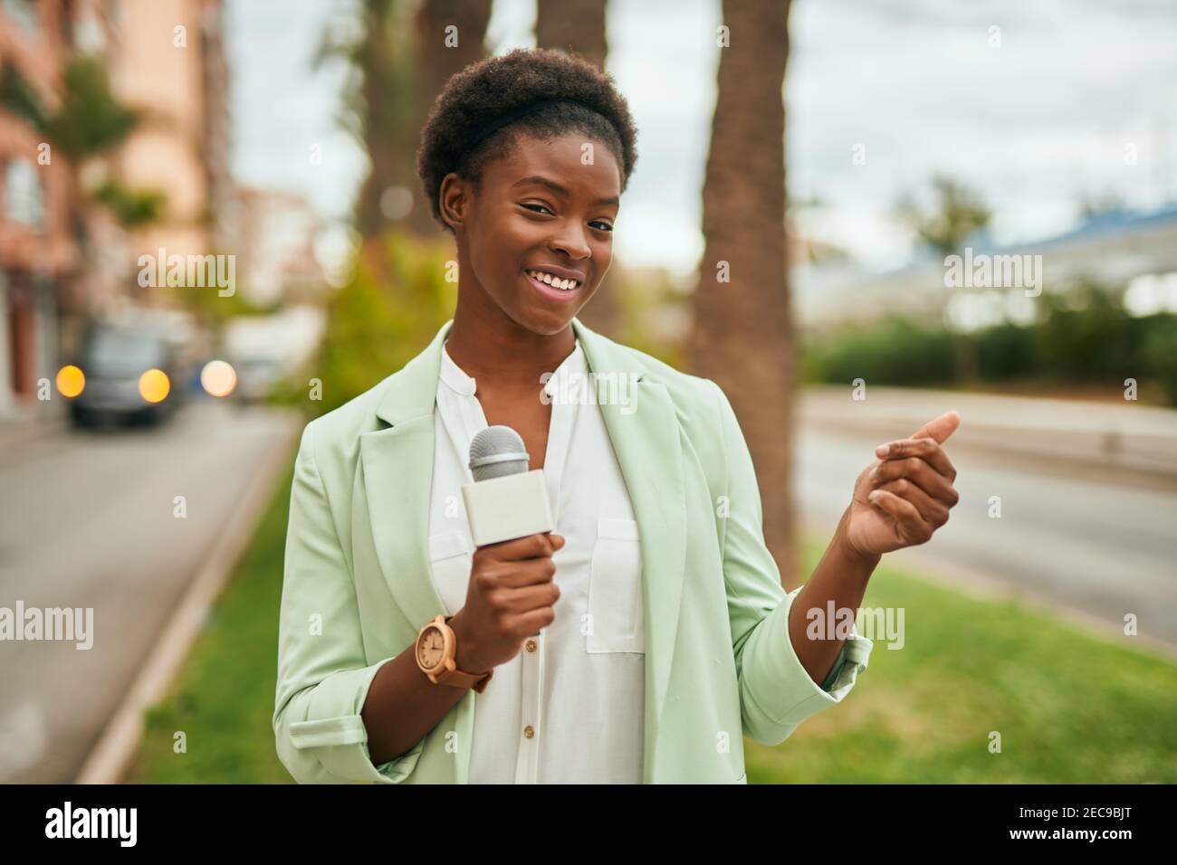 Young african american reporter woman using microphone at the city ...