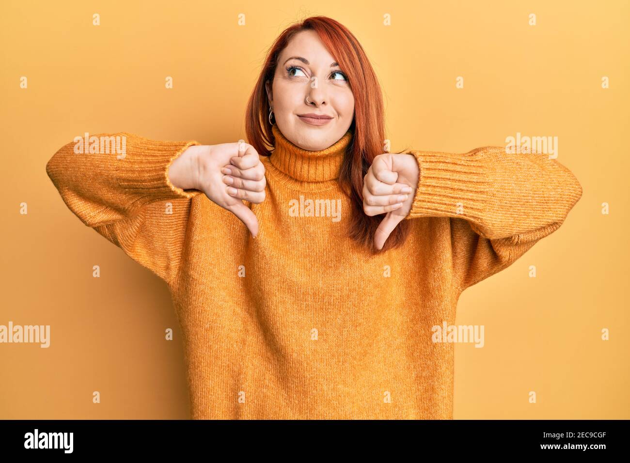 Beautiful redhead woman doing negative thumbs down gesture smiling ...