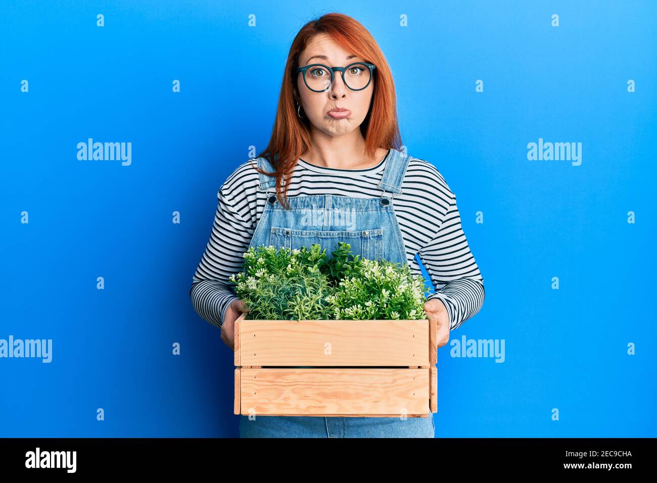 Beautiful redhead woman holding wooden plant pot depressed and worry ...
