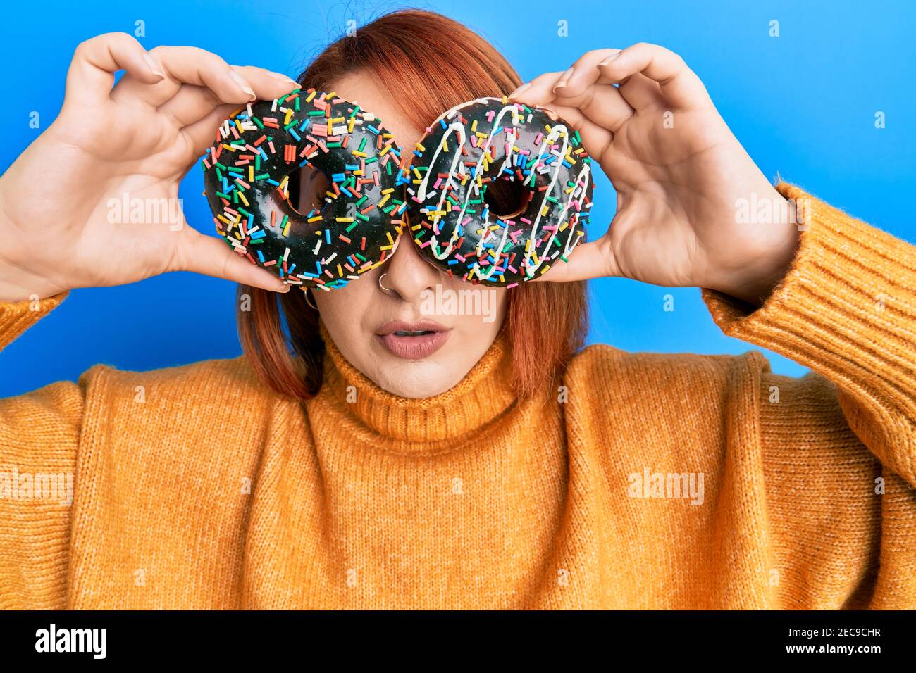 Beautiful redhead woman holding tasty colorful doughnuts on eyes ...