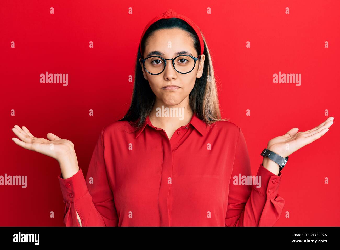 Young hispanic woman wearing casual clothes and glasses clueless and ...
