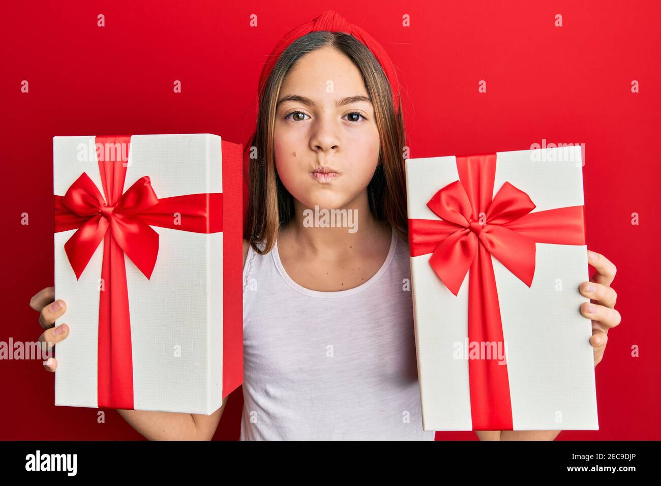 Beautiful brunette little girl holding gifts puffing cheeks with funny ...